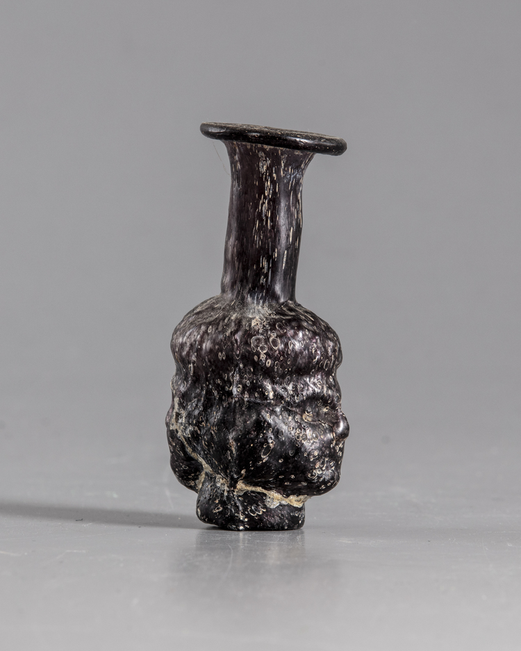 A ROMAN MOULDED PURPLE GLASS HEAD FLASK, CIRCA 3RD CENTURY AD